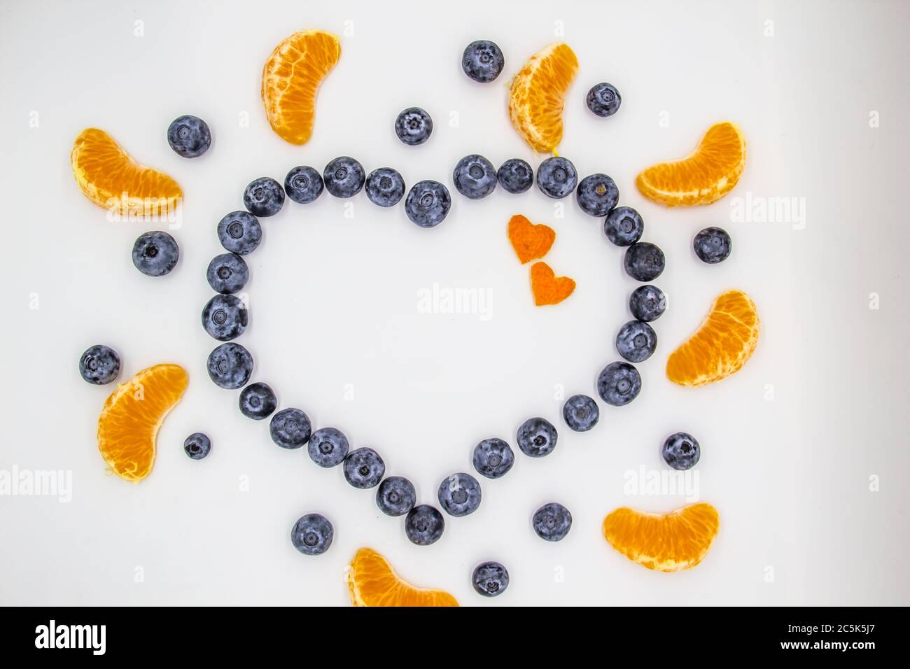 A heart's frame from mandarin pieces and blueberry on white background ...