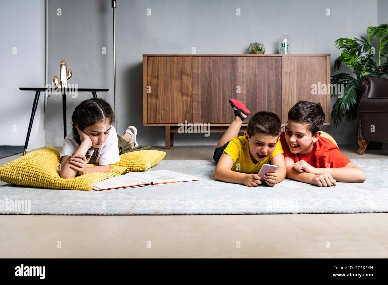 Little girl reading a book while two boys playing with a smart phone ...