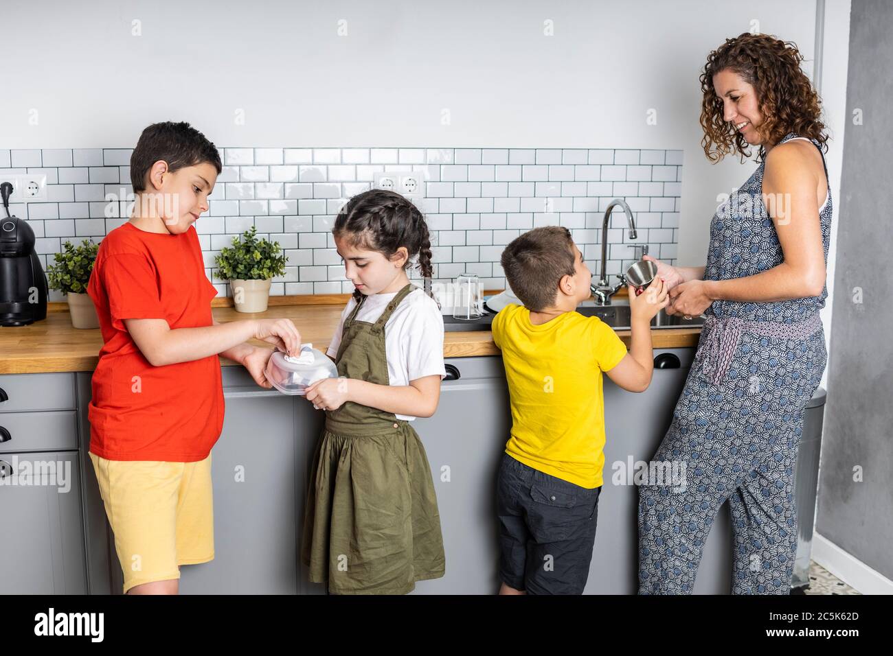 Three kids helping their mother clean the dishes Stock Photo - Alamy