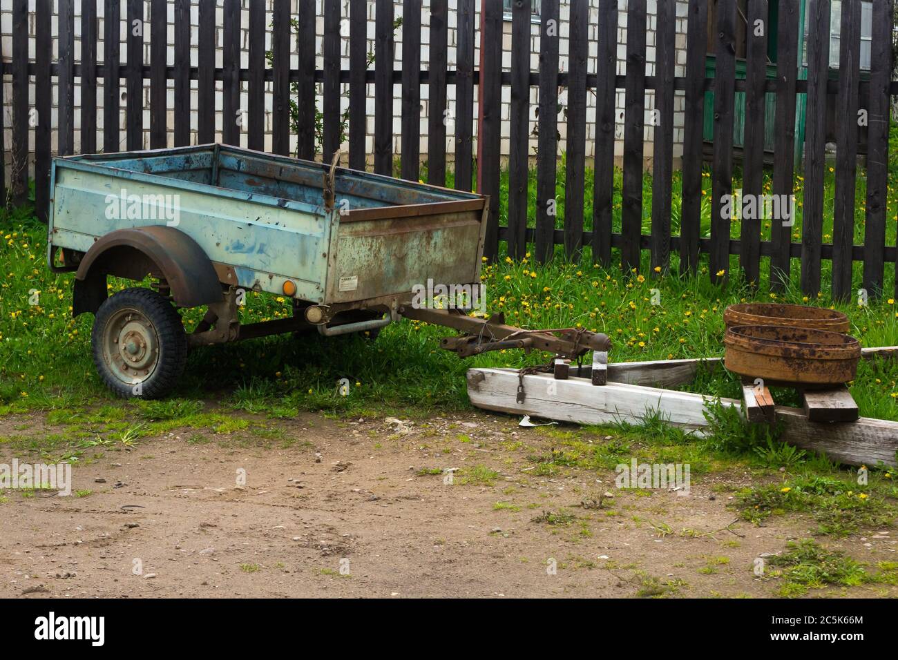 an old blue trailer stands in a village, old rusty rims hold it ...