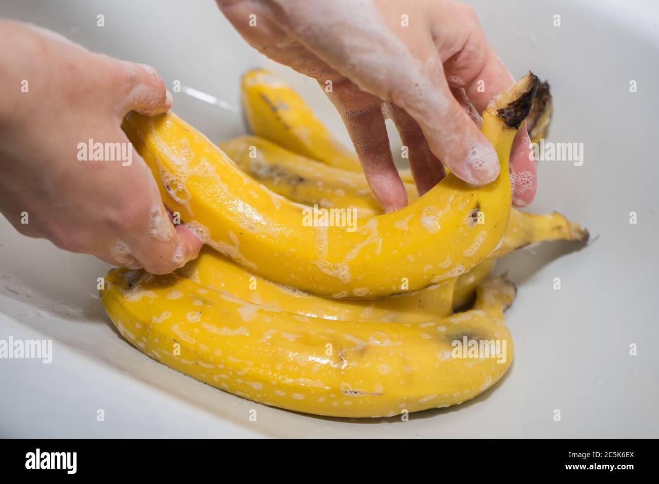Girl washes bananas with soap. Hands and soapy bananas in the sink ...