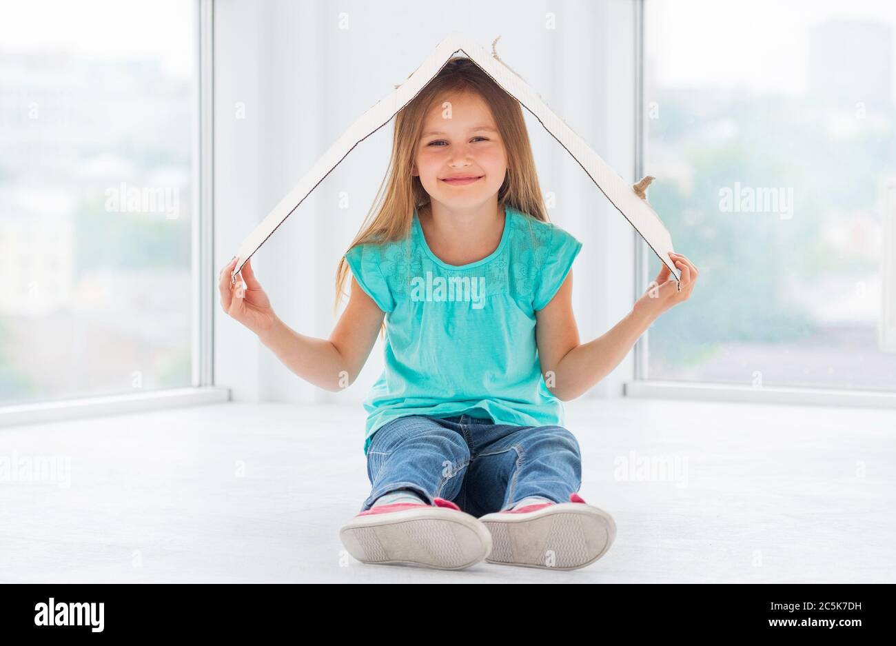 Beatiful kid girl is funny covering her head with piece of cardboard ...