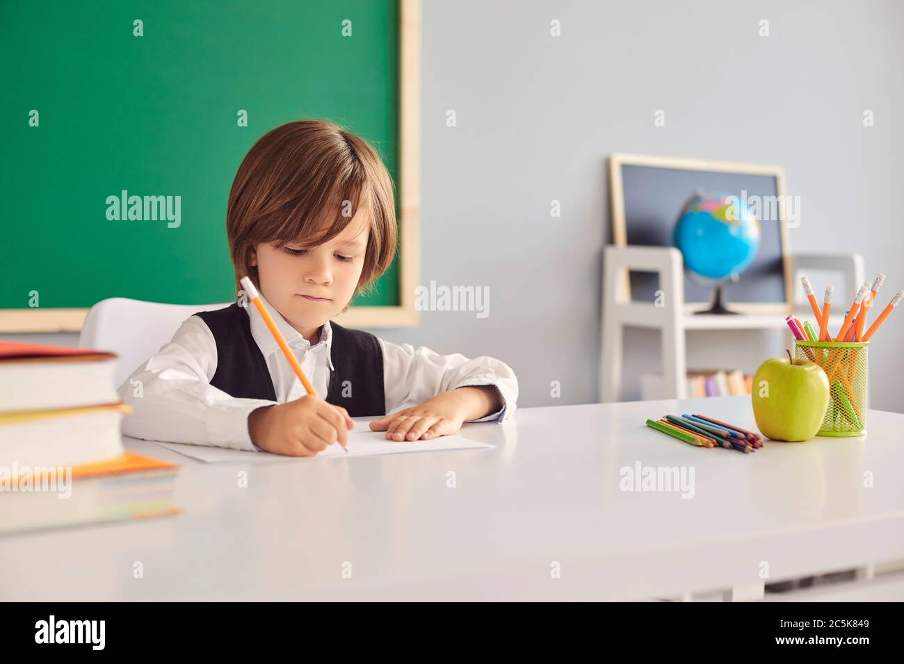Serious little boy drawing picture during art class at school, empty ...