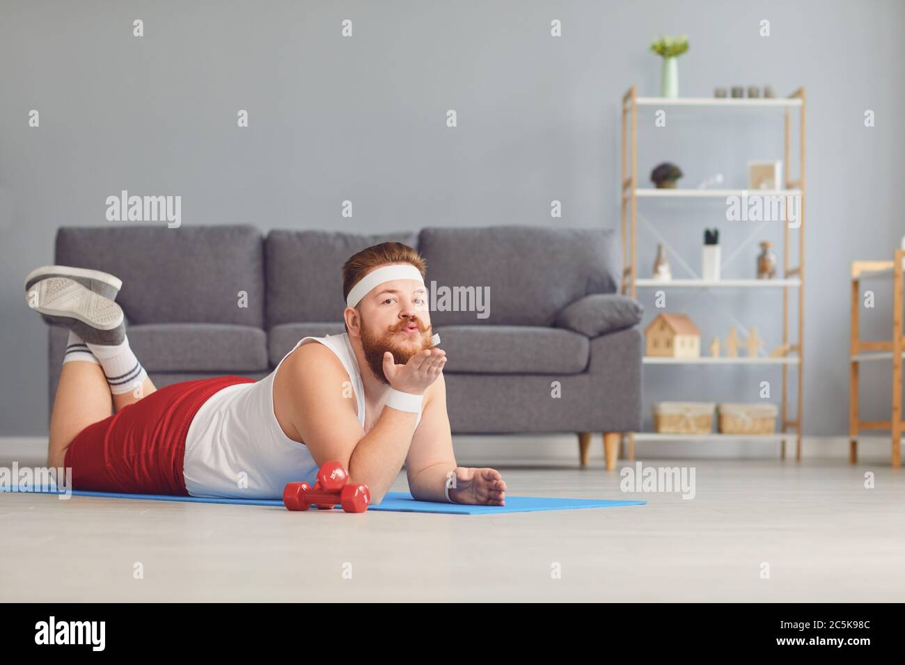 Funny red fat man doing exercises on the floor smiling while lying on ...
