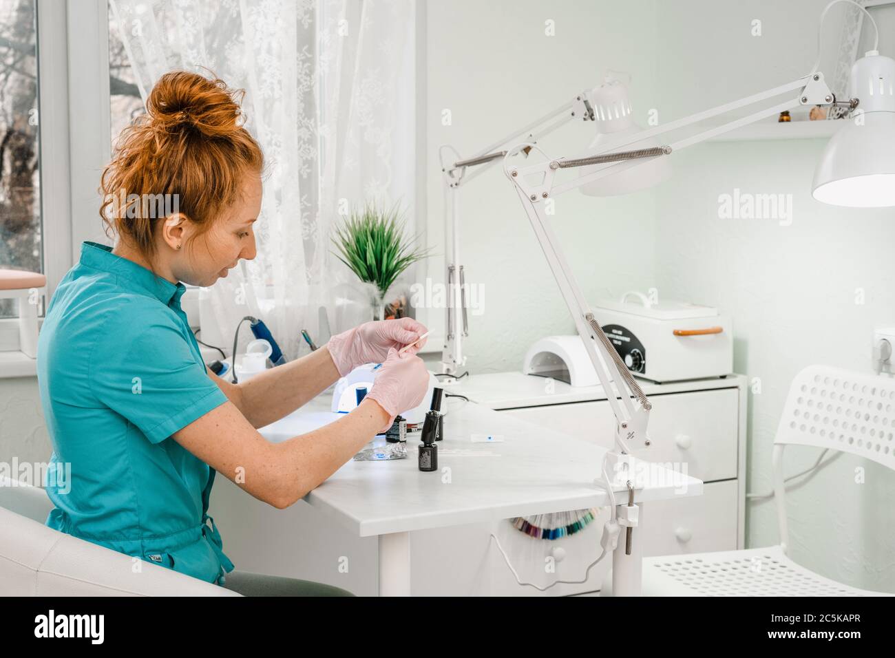 Manicurist at work in the office. Drawing gel polish on tips, creating ...