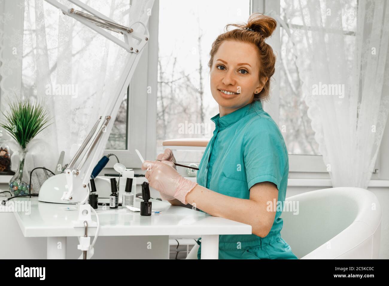Manicurist at work in the office. Drawing gel polish on tips, creating ...
