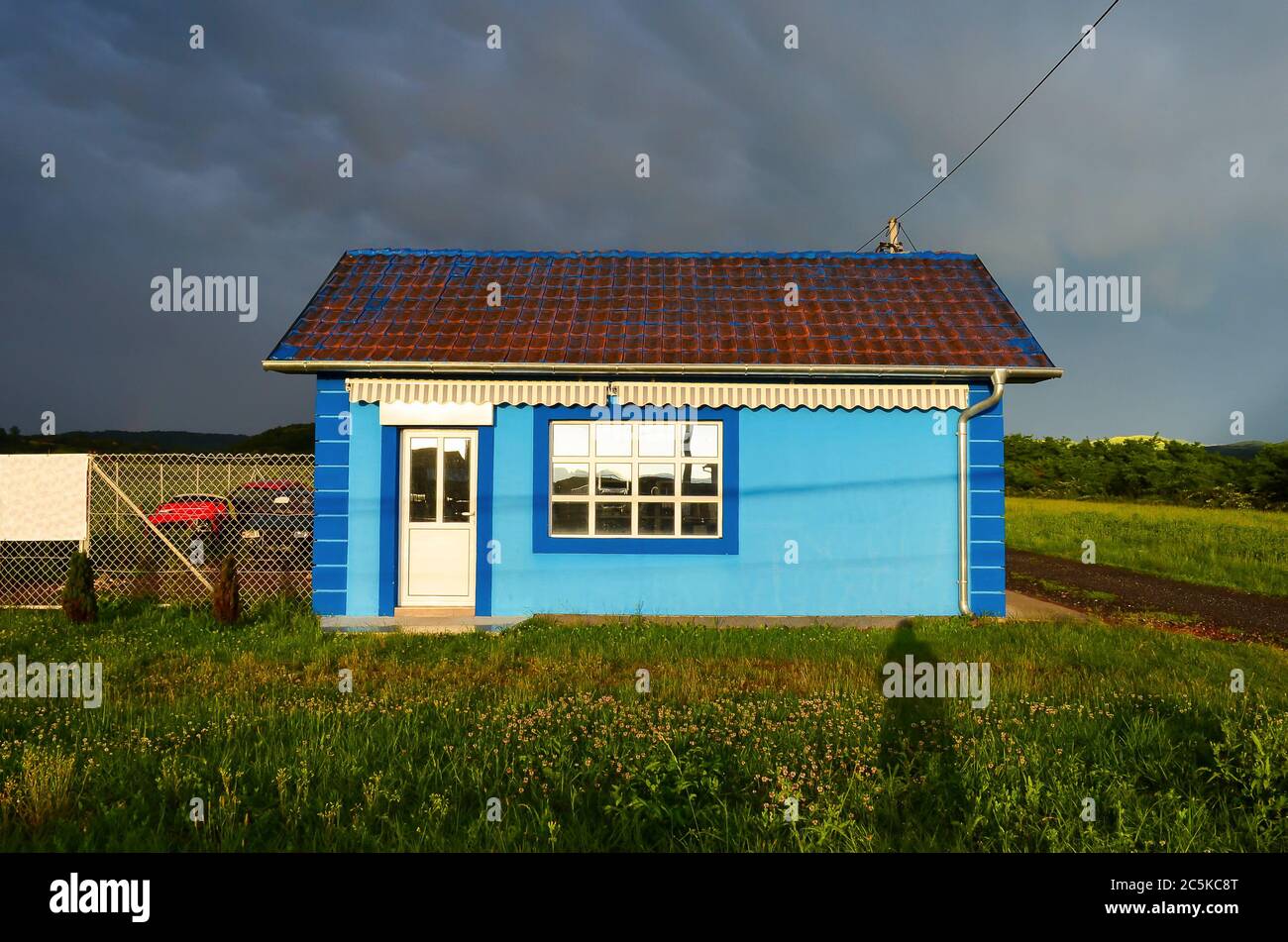 Small blue house in golden sunset light under dark clouds after summer ...
