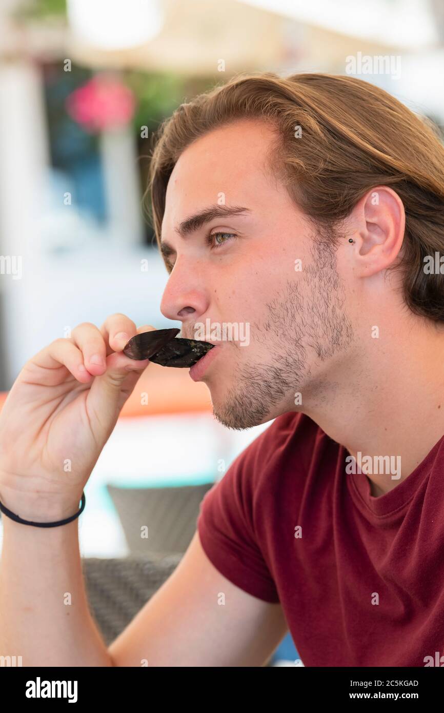 Close up of a handsome young man eating a mussel from its shell on an ...