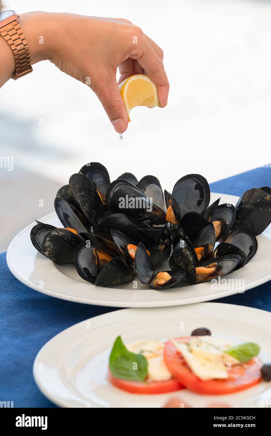 Hand squeezing a lemon slice over some delicious looking boiled mussels ...