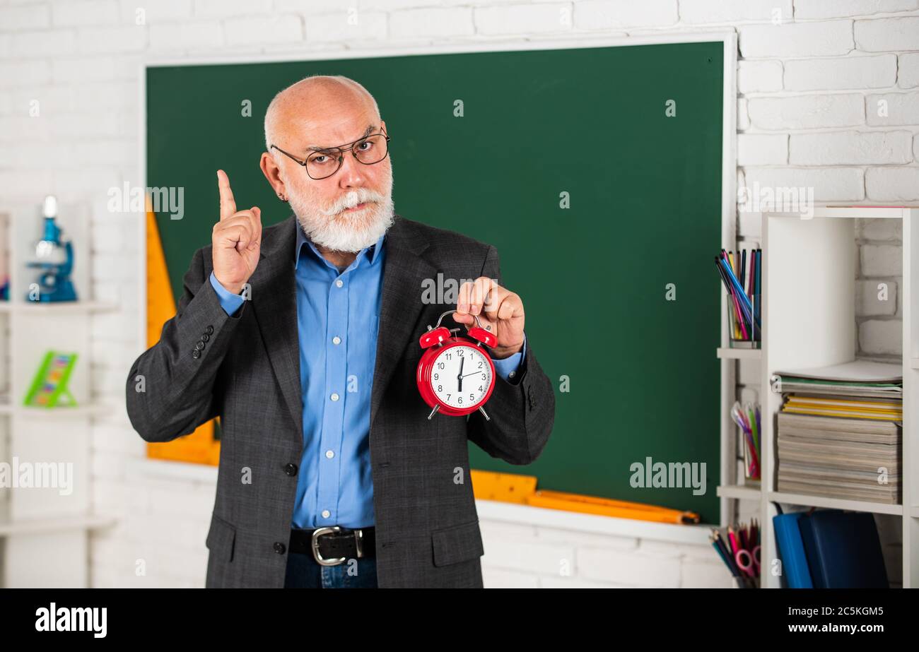 time to study. discipline and punctuality. senior teacher hold alarm ...