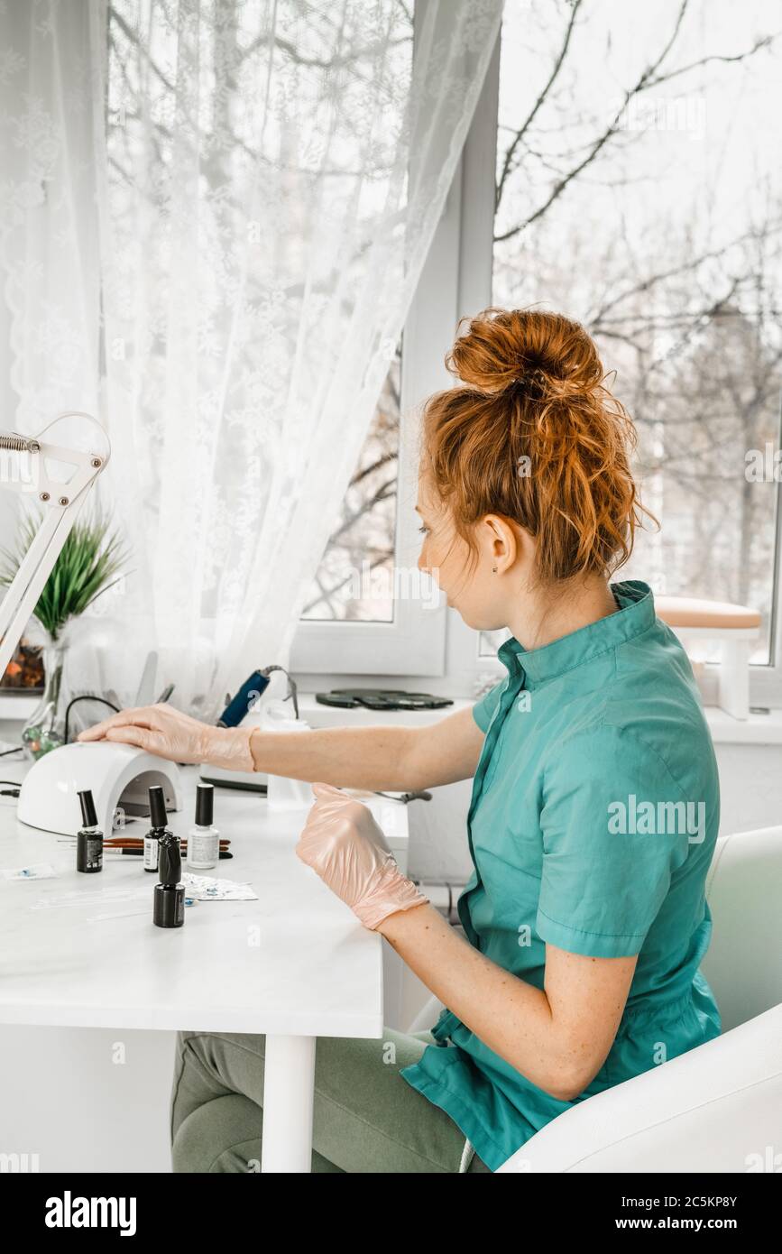 Manicurist at work in the office. Drawing gel polish on tips, creating ...