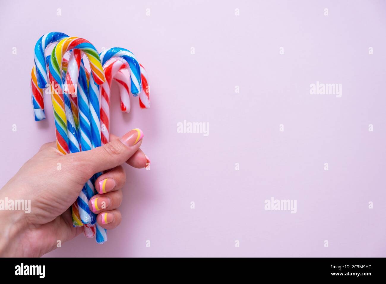 female hand holds a lot of multi-colored candy canes on a pink ...