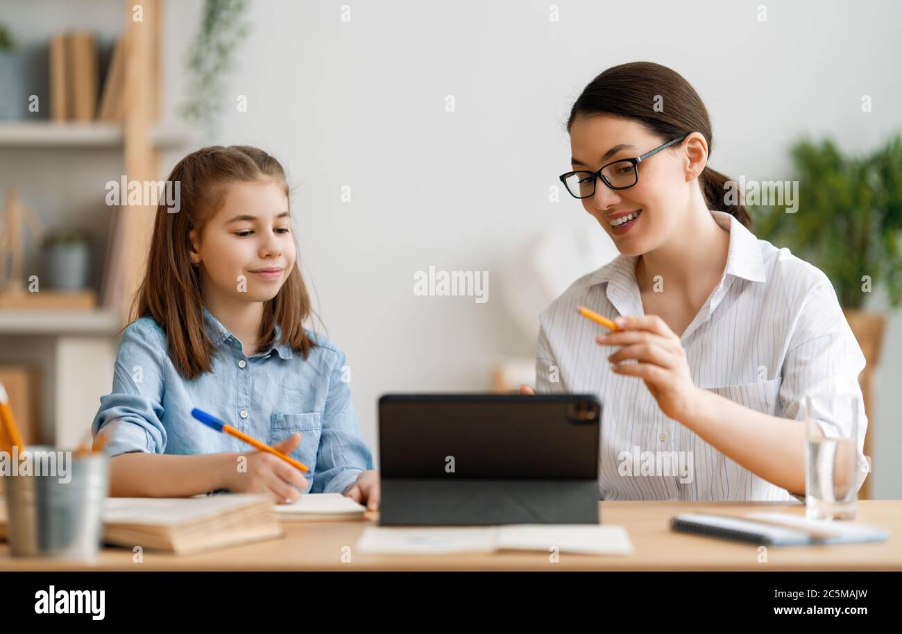 Back to school. Happy child and adult are sitting at desk. Girl doing ...
