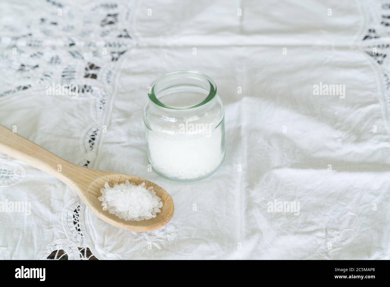 Wooden spoonful of sea salt or rock salt with bottle of salt on white ...