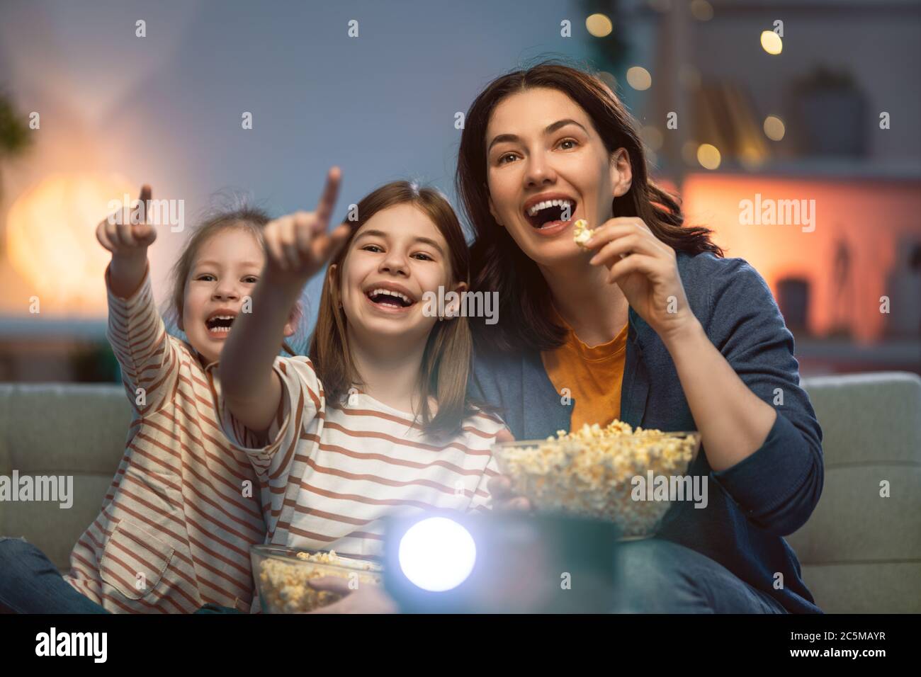 Happy family watching projector, TV, movies with popcorn in the evening ...