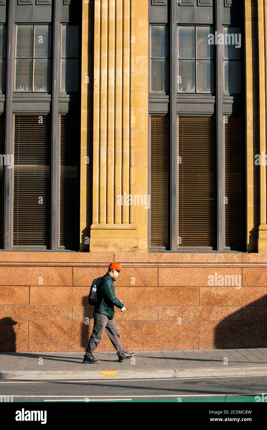 Traveling man walking on a city street past a large yellow building ...