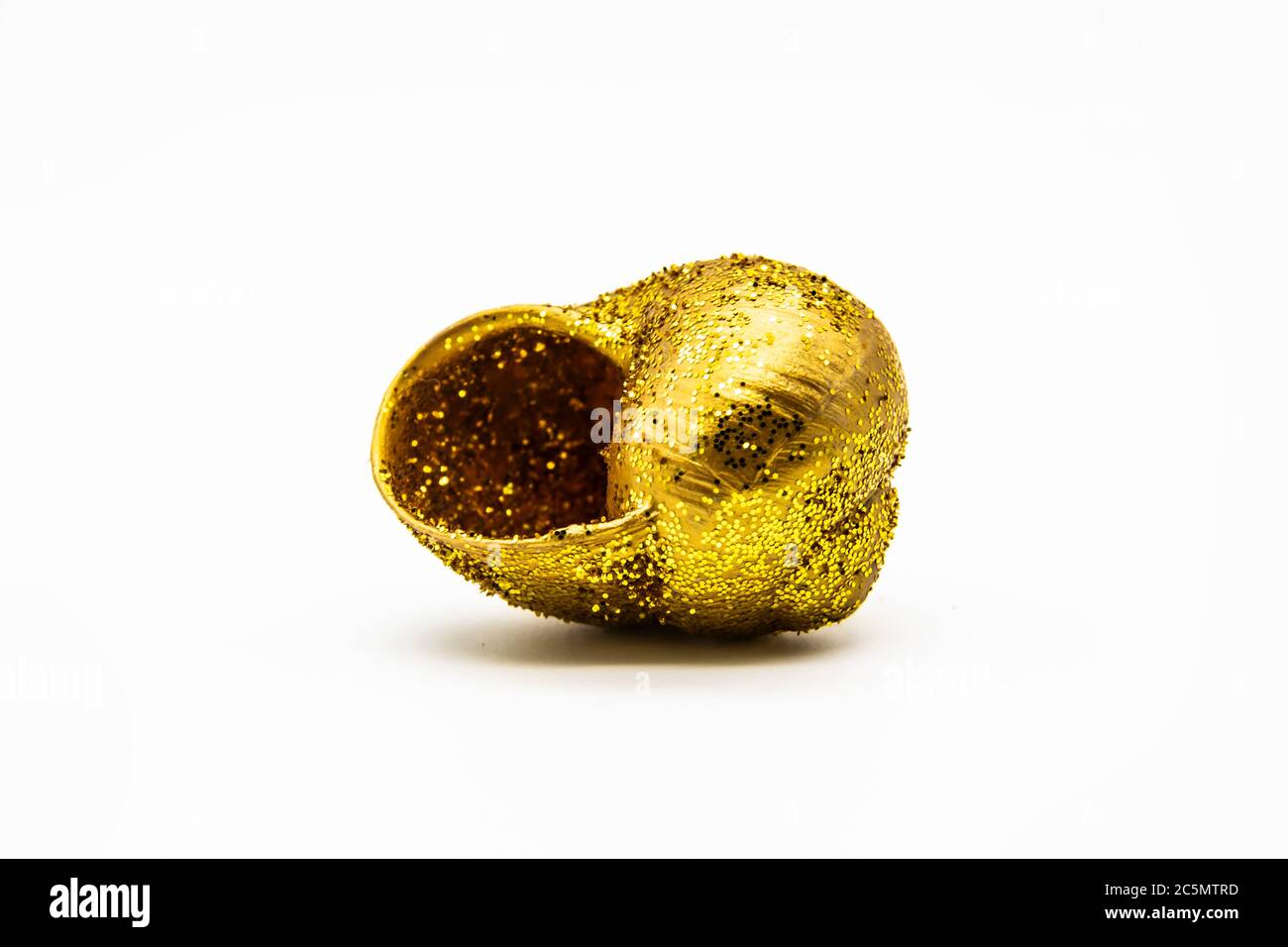 Empty shell of a snail in the gold glitter against white background ...