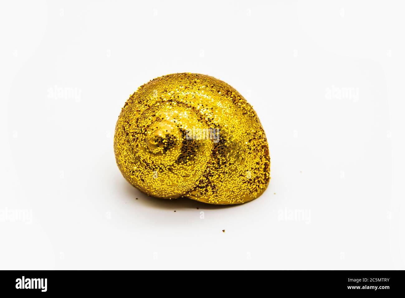 Empty shell of a snail in the gold glitter against white background ...