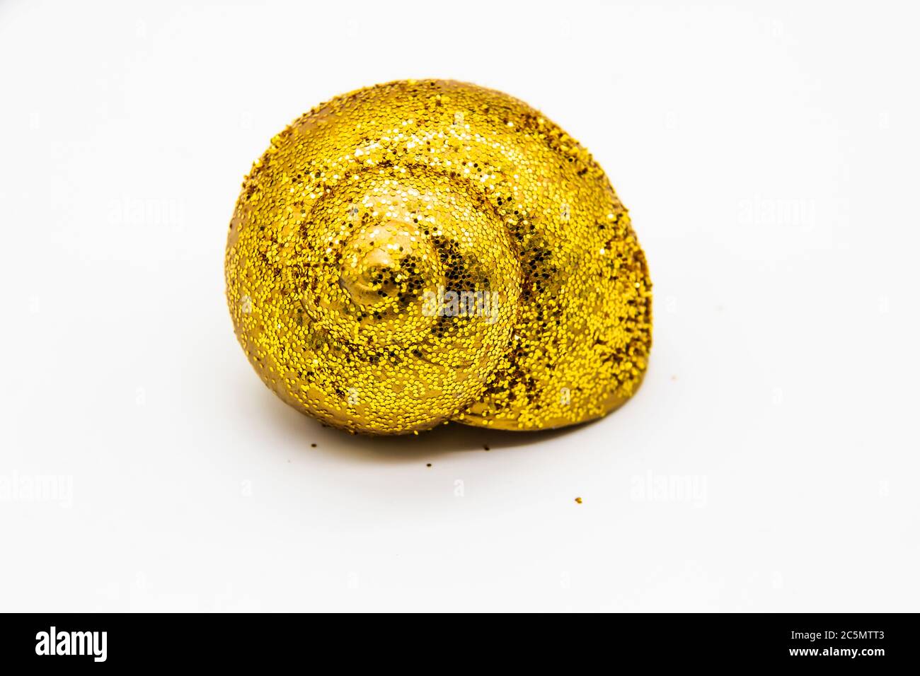Empty shell of a snail in the gold glitter against white background ...