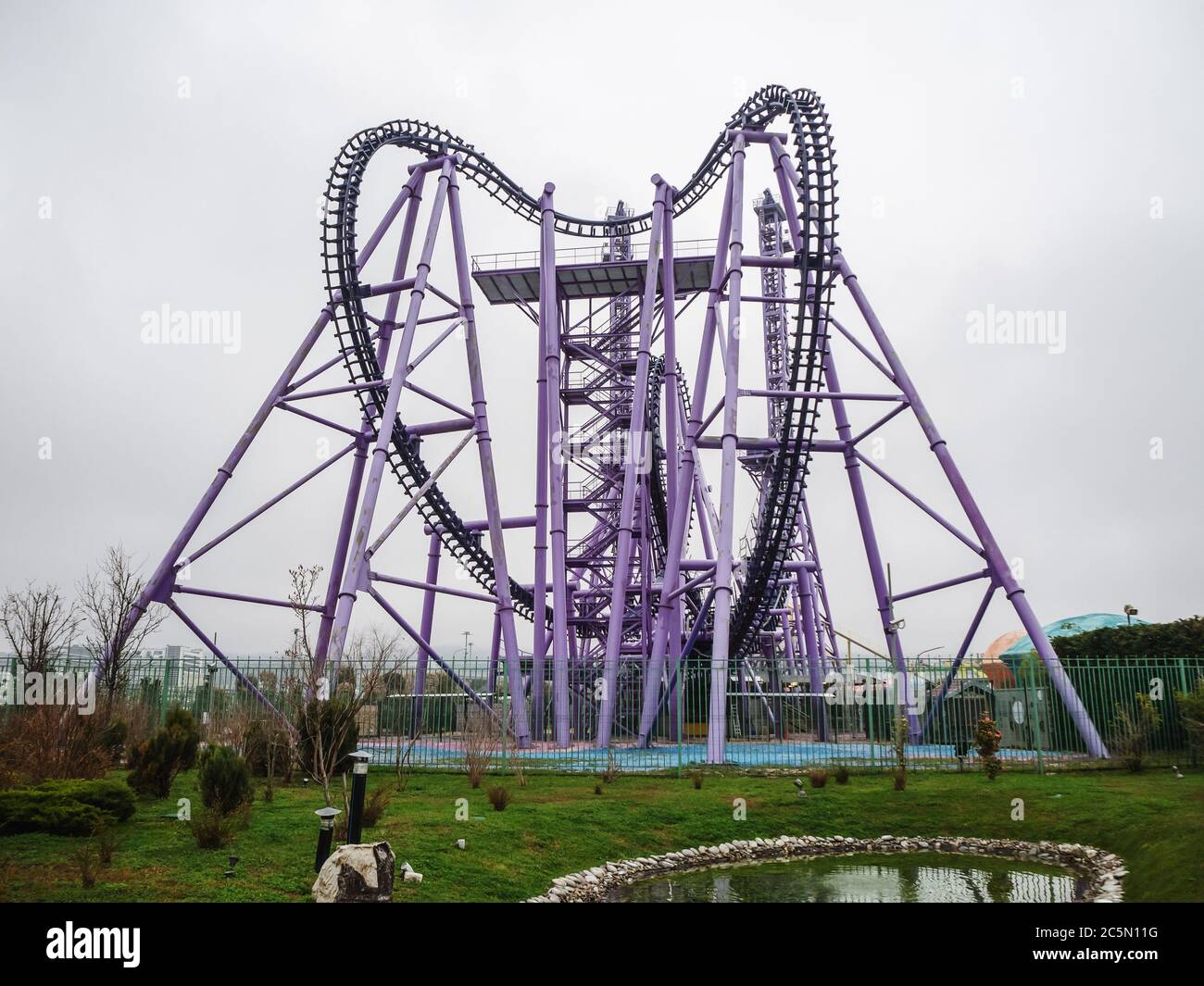 Large lilac amusement ride roller coaster on the plain fenced by a blue ...
