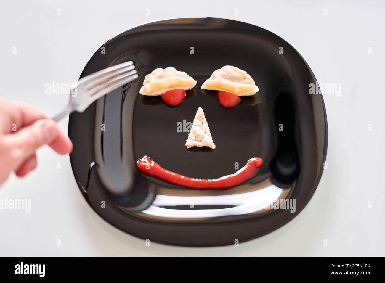 Funny food face, dumpling and ketchup. Food art on black plate. Smiling ...