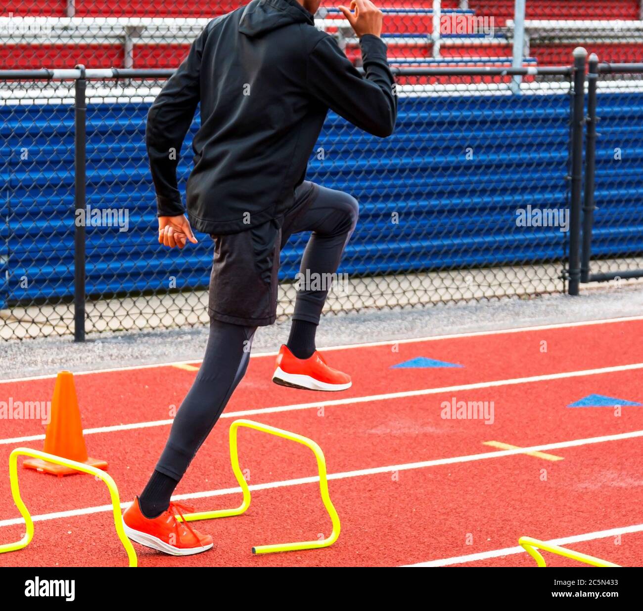 A high school track runner is stepping over yellow mini hurdles during ...