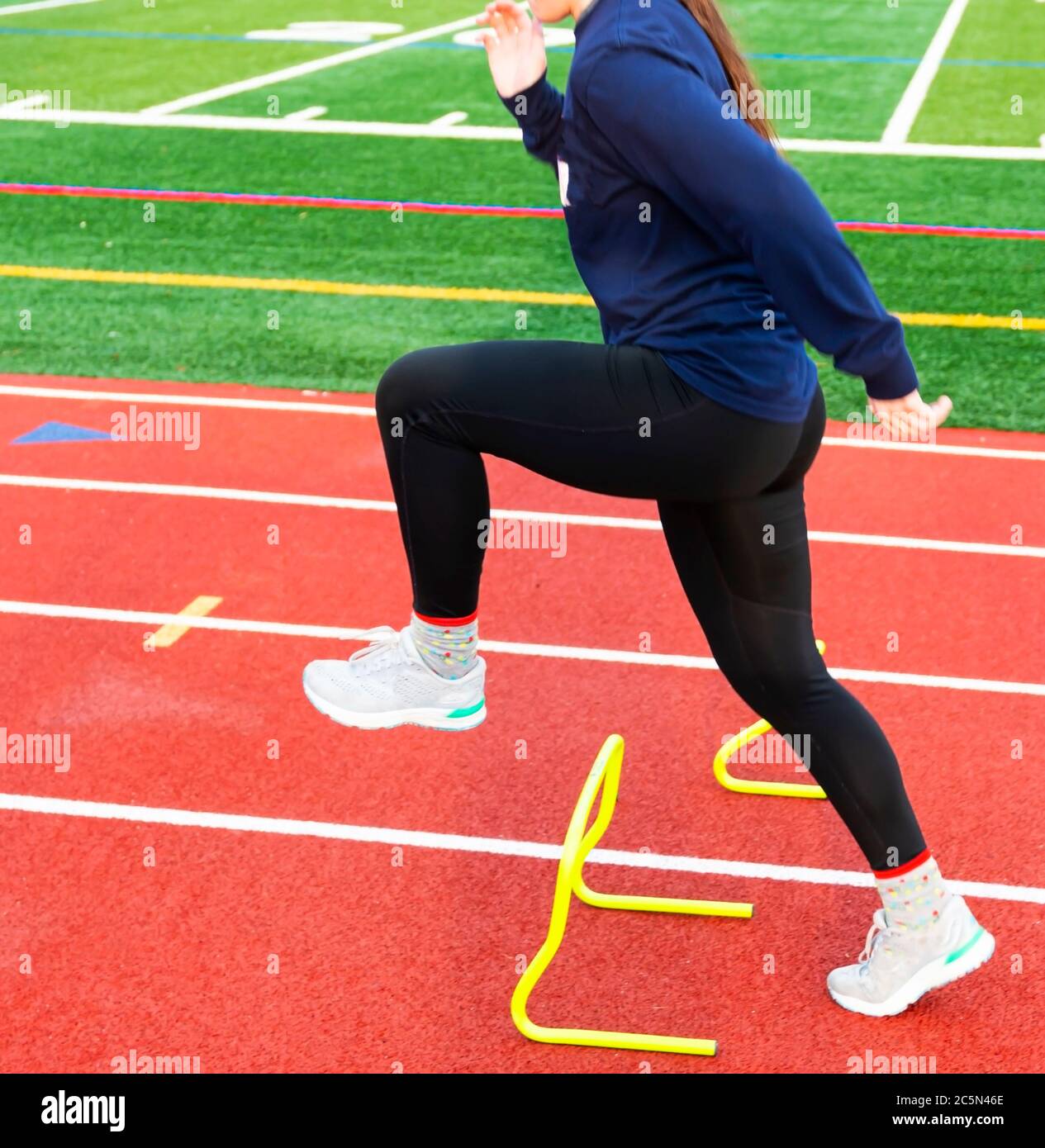 A high school teenage girl is stepping over yellow mini banana hurdles ...