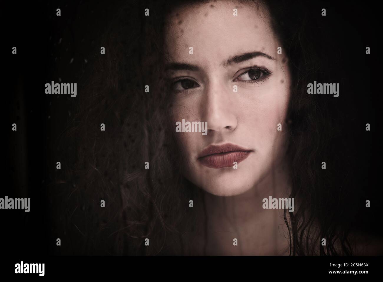 Pensive beautiful woman behind wet window Stock Photo - Alamy