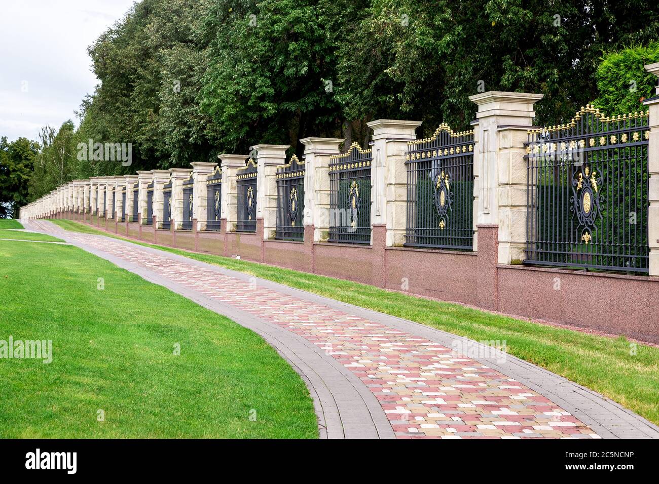 tile footpath and green grass along a stone fence with an iron grate in ...