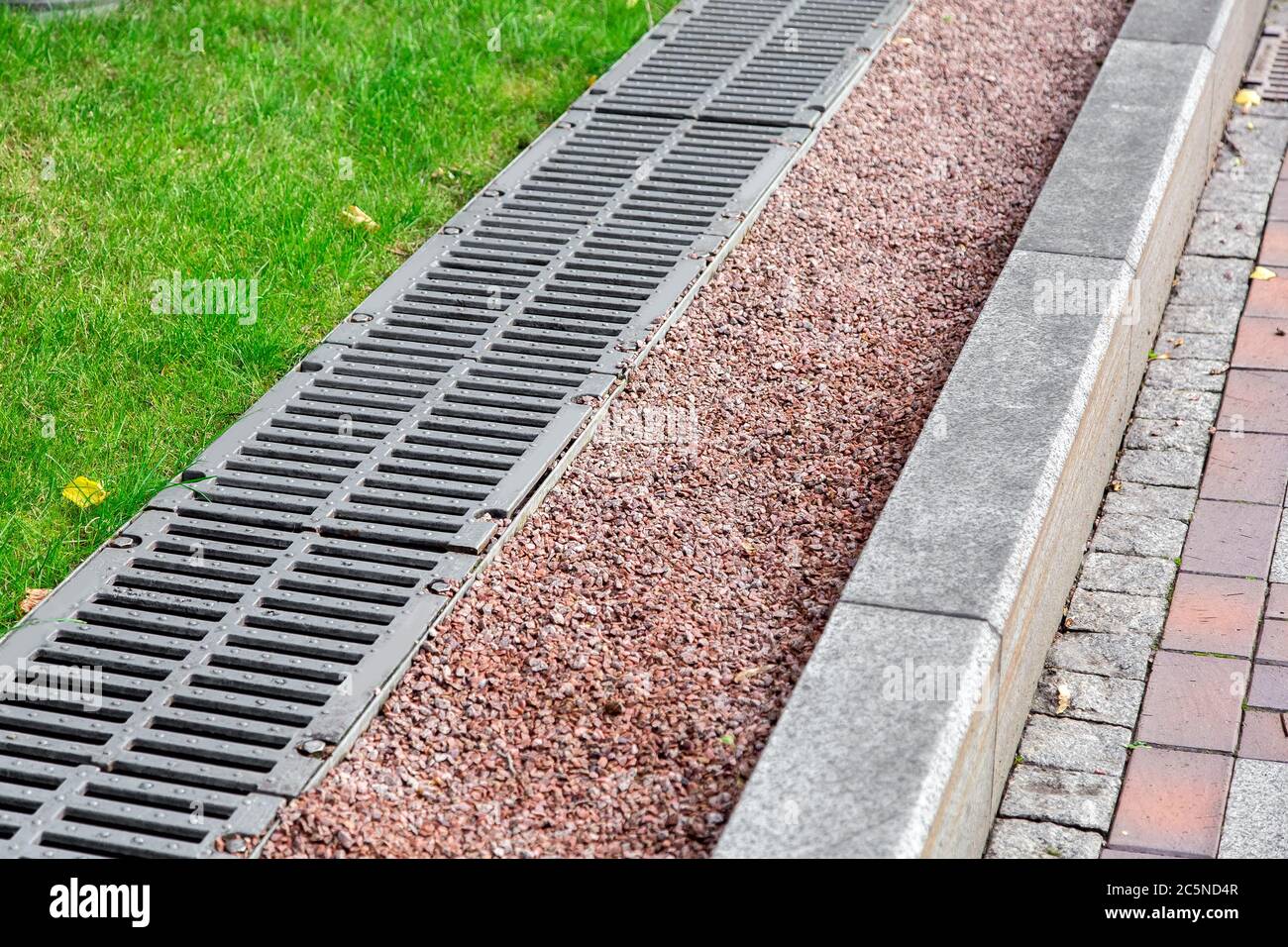 drainage system on the side of the road behind a border of pebbles and ...