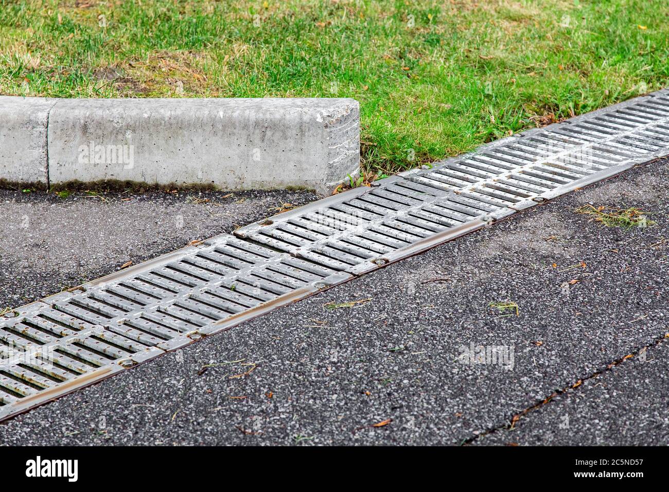 iron grid drainage system on an asphalt road with a curb on the side of ...