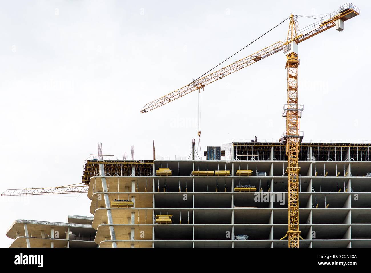 A yellow tower crane lifts building materials to the top of a multi ...