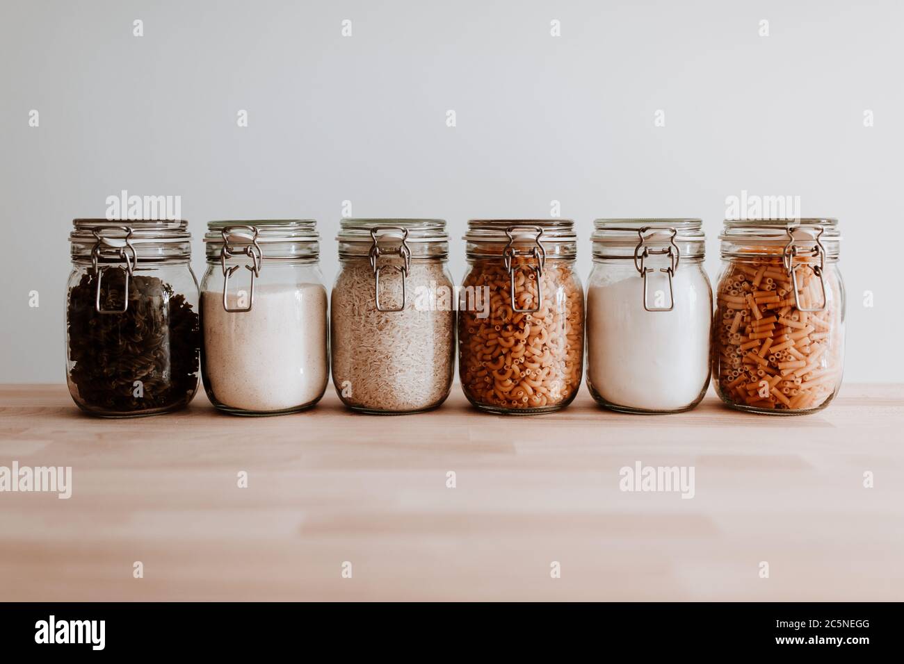 Six glass jars full with dried uncooked food ingredients on wooden ...