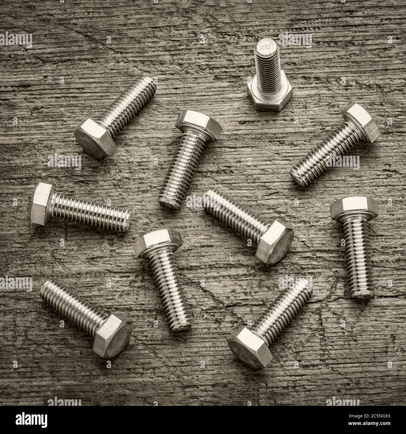 a set of ten hex stainless steel bolts against rustic wood, black and ...
