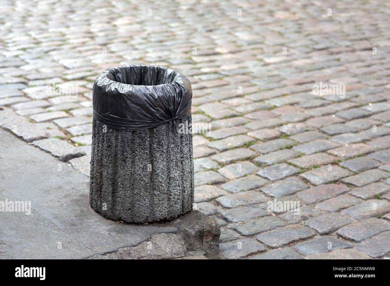 Trash bag in a concrete bin mounted on a pedestrian pavement of paving ...