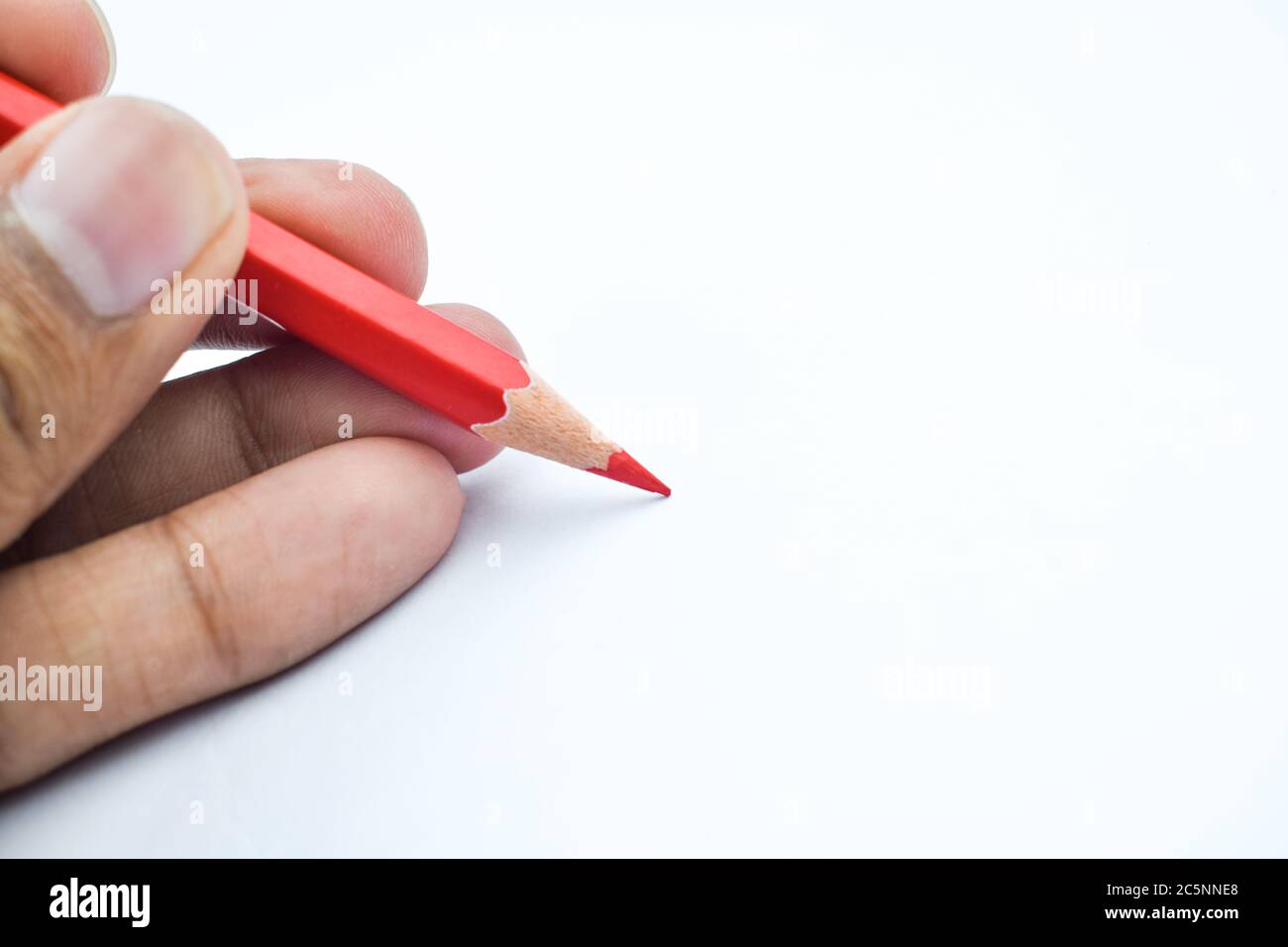 A man writing with a red pencil crayon with a sharp tip on a white ...