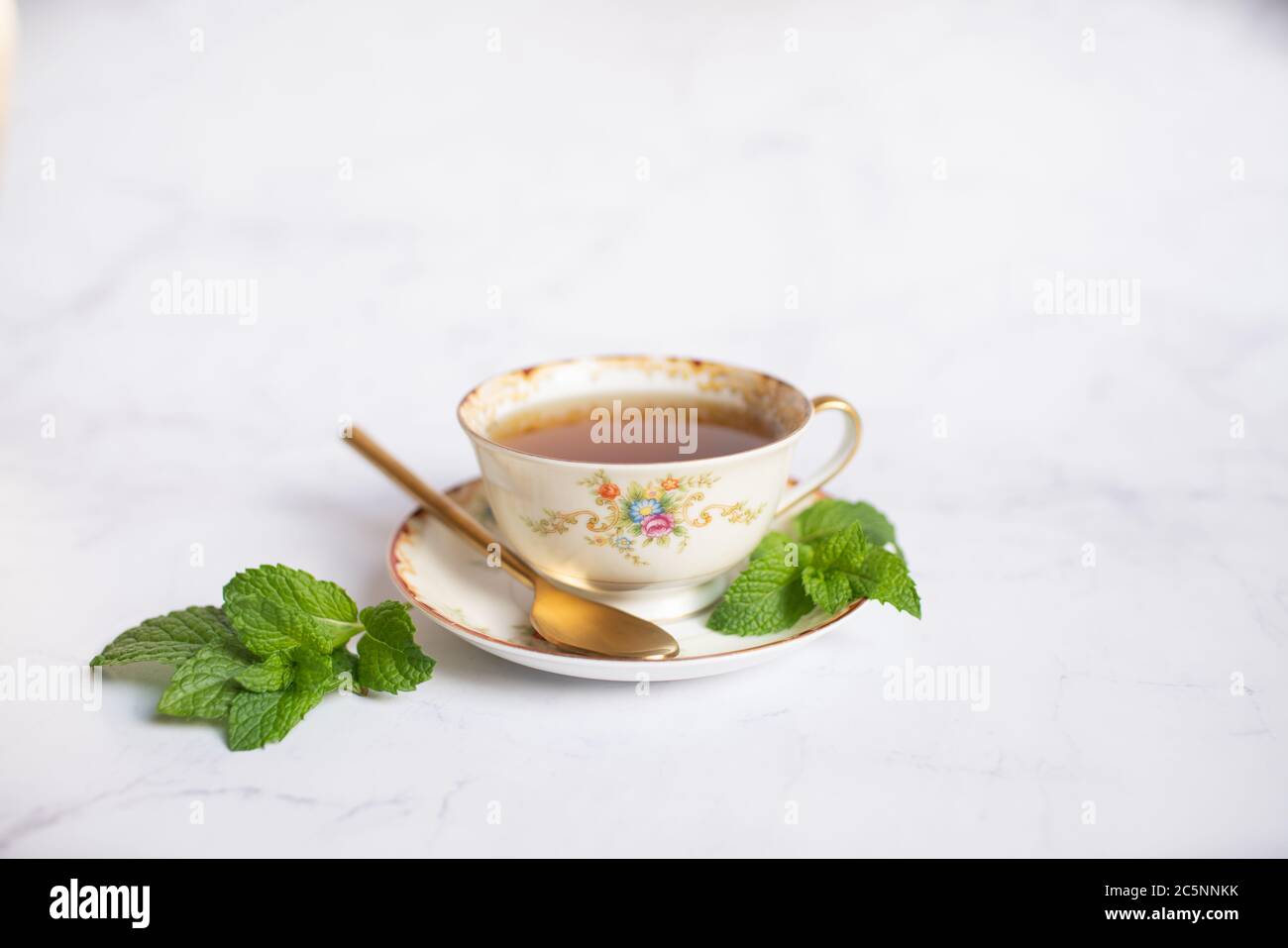 Traditional mint tea cup with spoon and fresh mint on a white marble ...