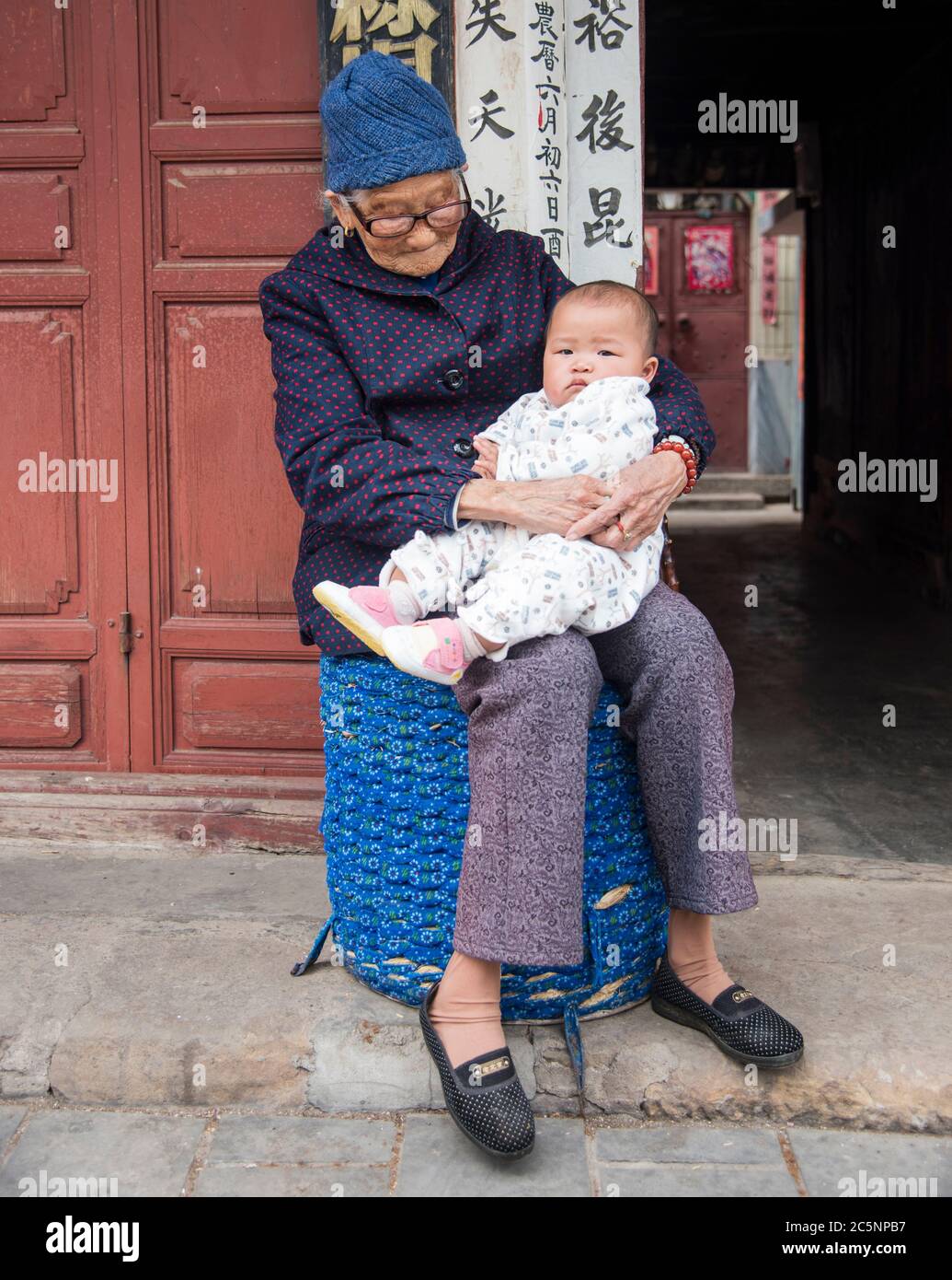 Old Chinese grandmother sitting down and holding baby granddaughter in ...
