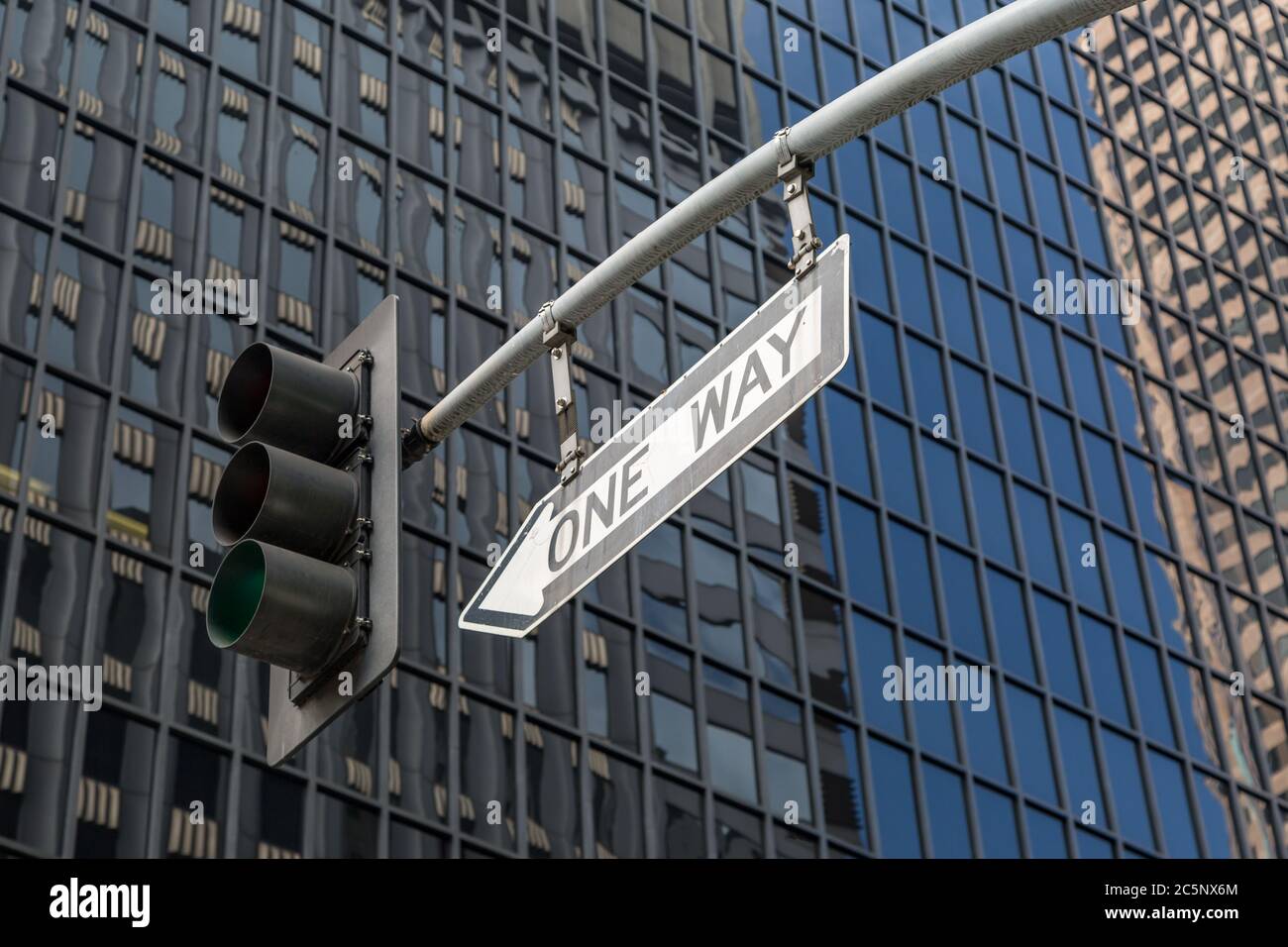 Looking up at a One Way sign and traffic lights, with buildings behind ...