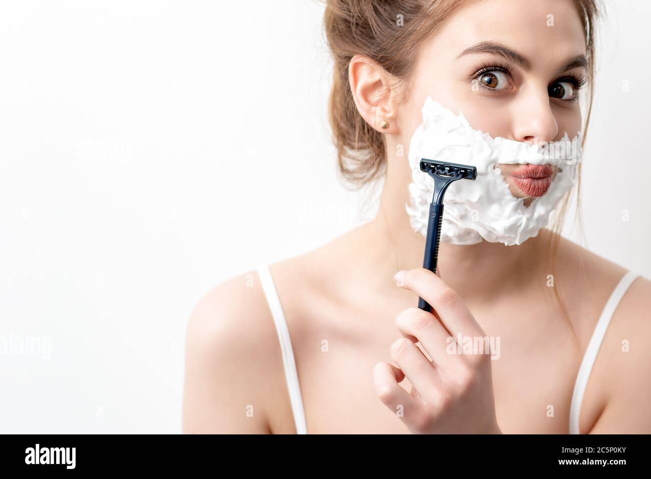 Beautiful young caucasian woman shaving her face by razor on white background. Pretty woman with ...