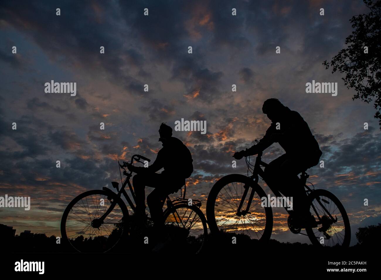 Two cyclists in a London park ride under a dramatic sunset Stock Photo ...