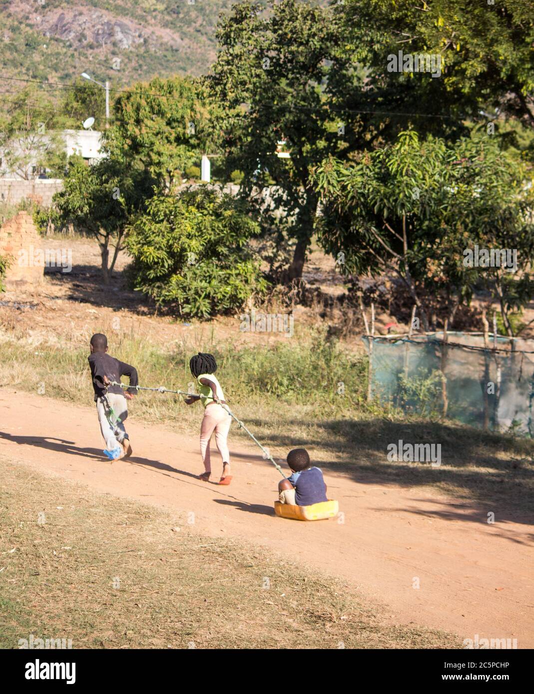 African children pulling small boy on recycled plastic sled with rope ...