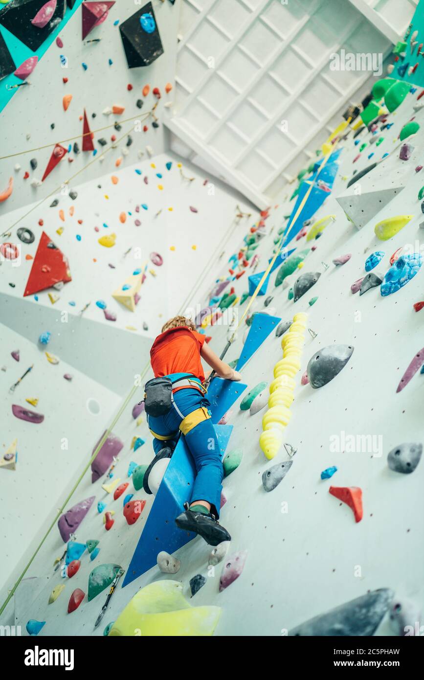 Teenager boy at indoor climbing wall hall. Boy is climbing using a top ...