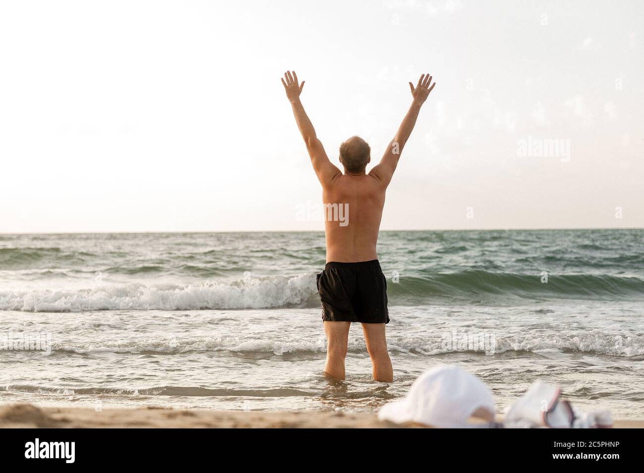 A young man prepares to bathe in the sea, holding a T-shirt which he ...