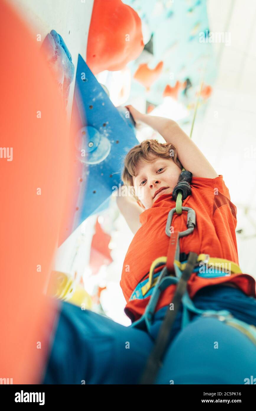 Teenager boy at indoor climbing wall hall. Boy is climbing using a top ...