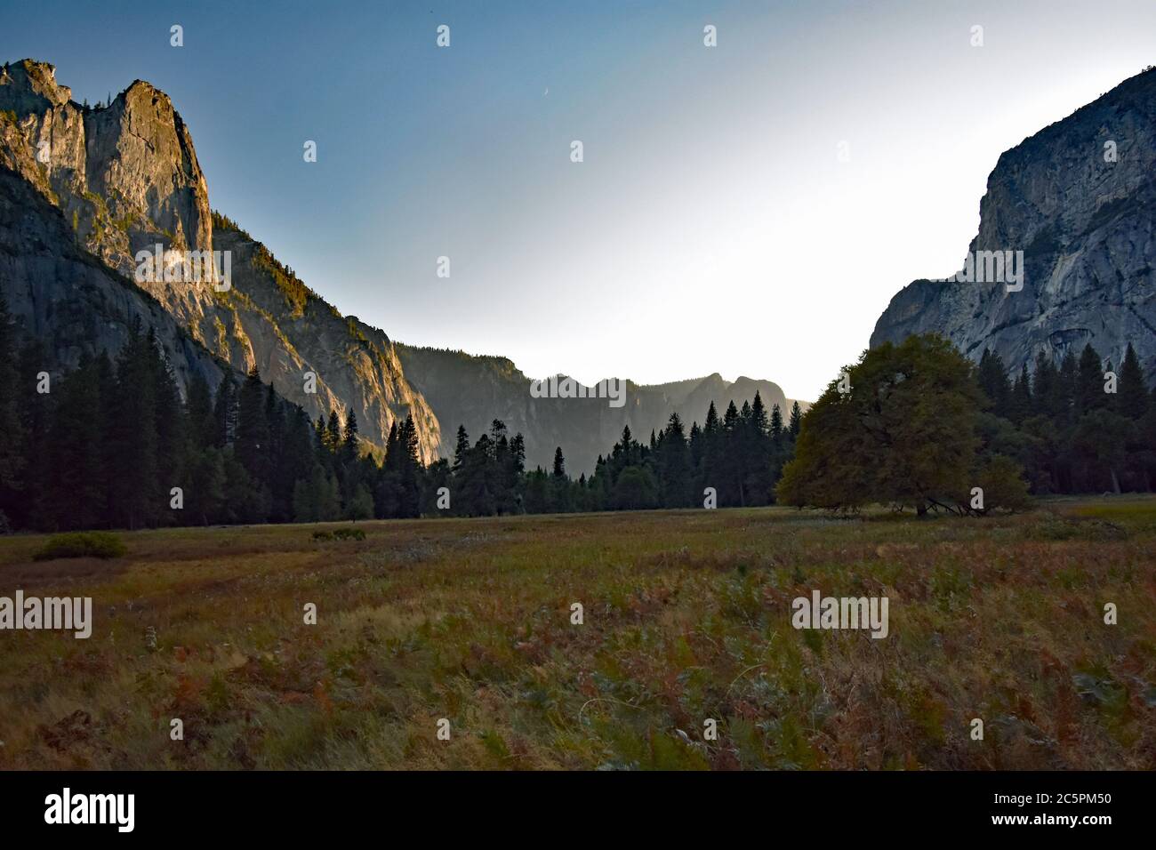 A meadow iYosemite Valley at sunset, surrounded by tall granite cliffs ...