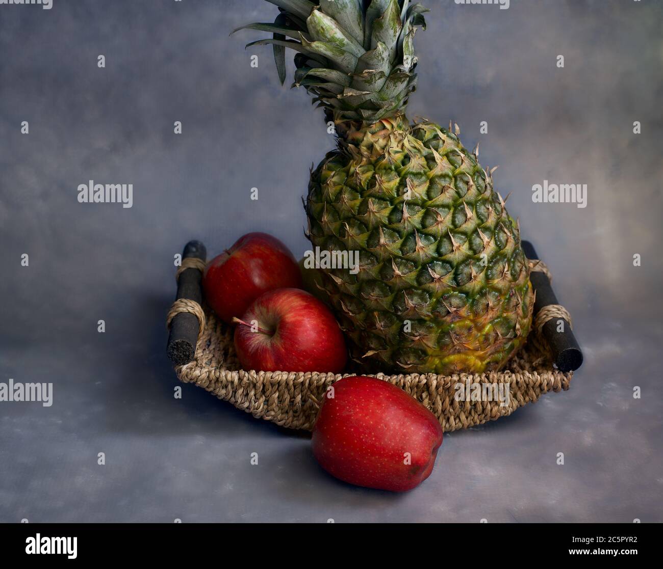 Pineapple in a basket with three red apples Stock Photo - Alamy