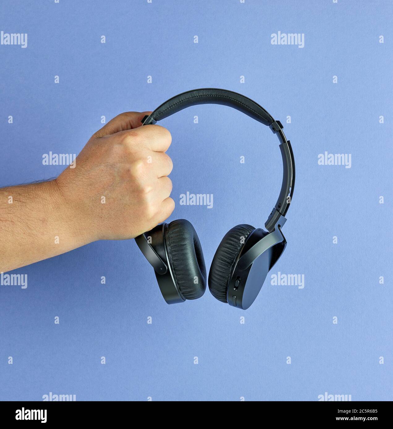 Black wireless headphones in human hand on blue background Stock Photo ...