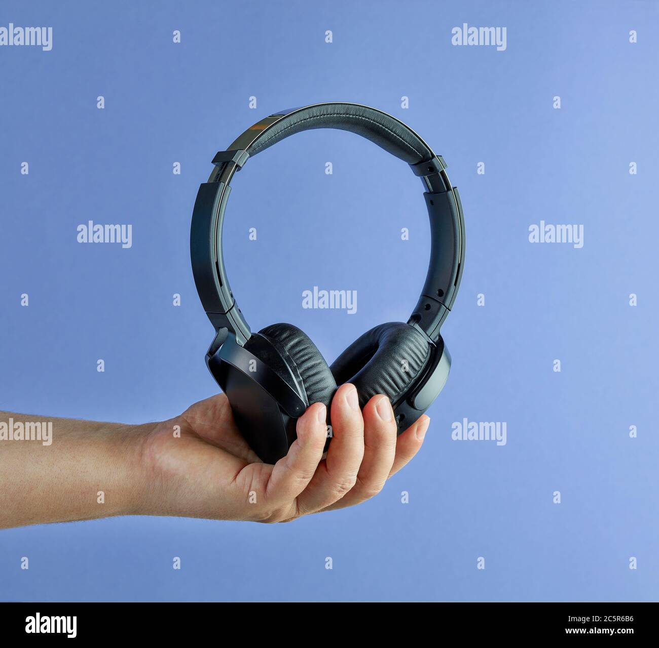 Black wireless headphones in human hand on blue background Stock Photo ...