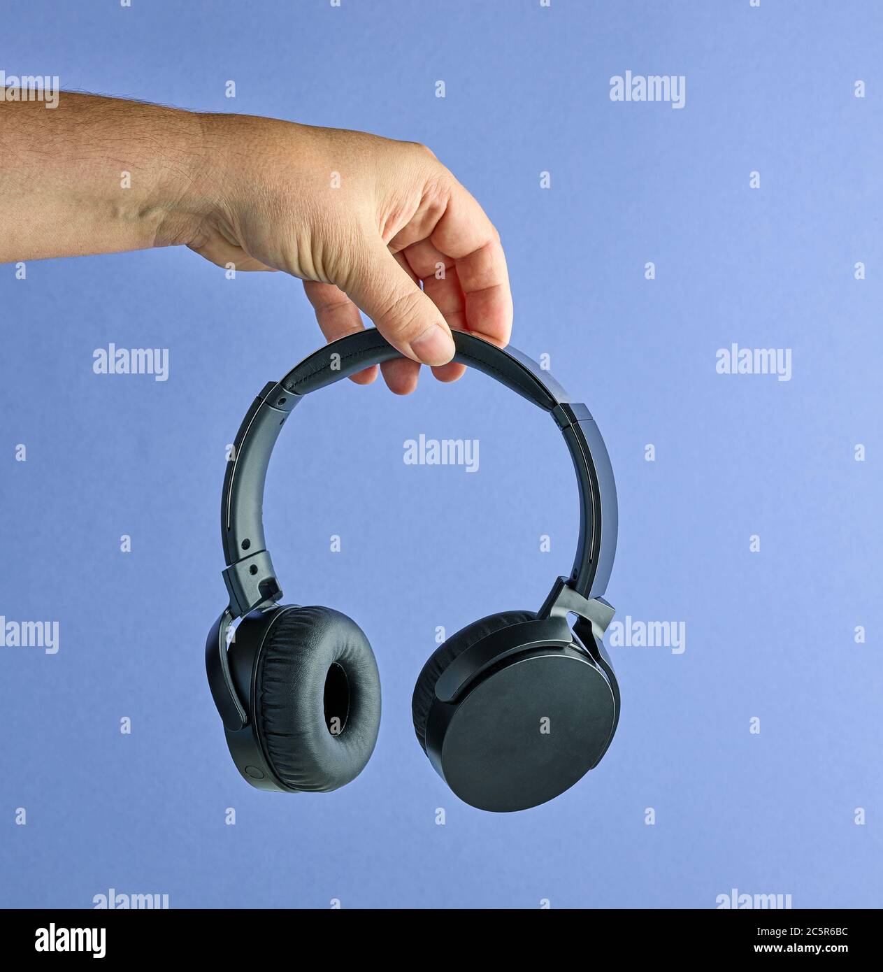 Black wireless headphones in human hand on blue background Stock Photo ...